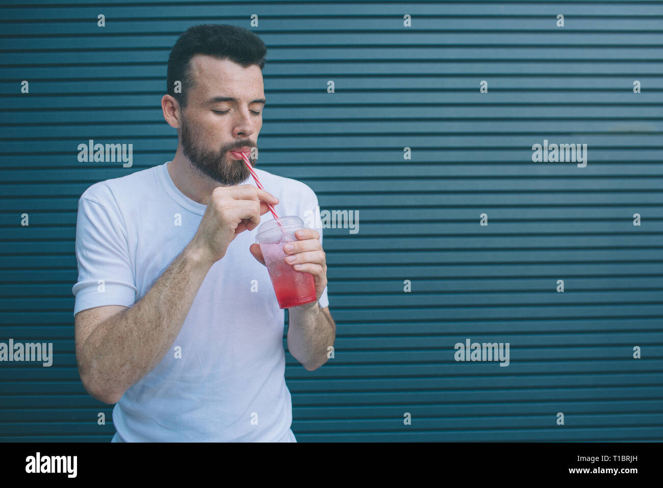Bearded man is drinking lemonade from plastic cup through straw. He is ...