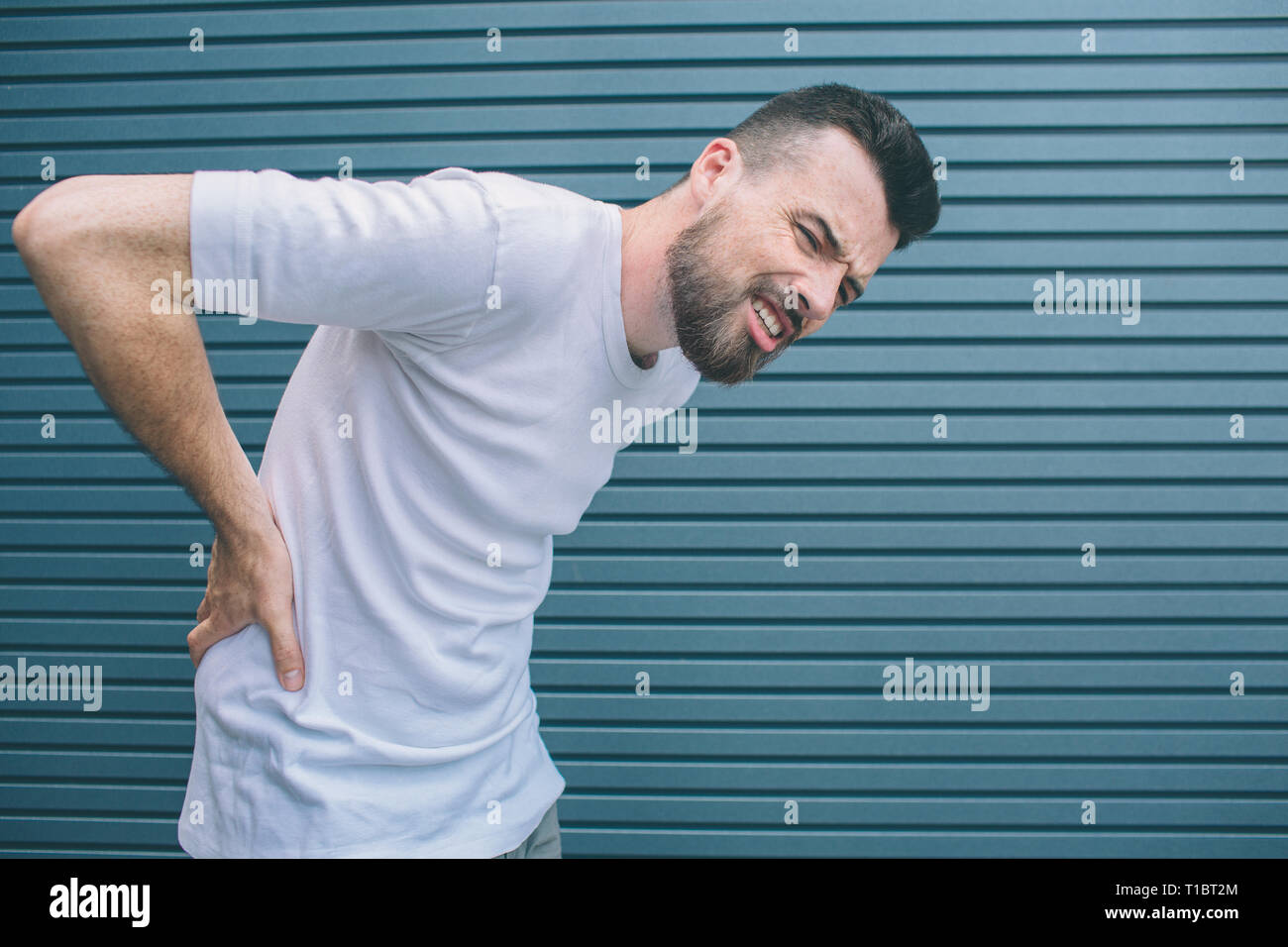 Unhappy guy is suffering from back pain. He is holding hands on spine ...