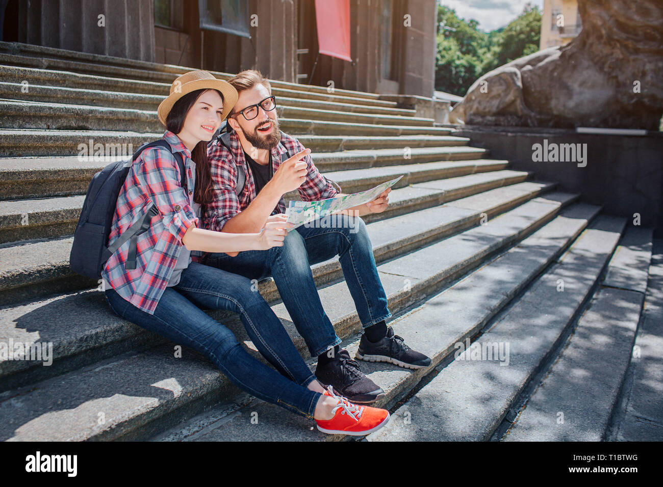 Tourists sit on steps and look forward. Young man points. They smile ...