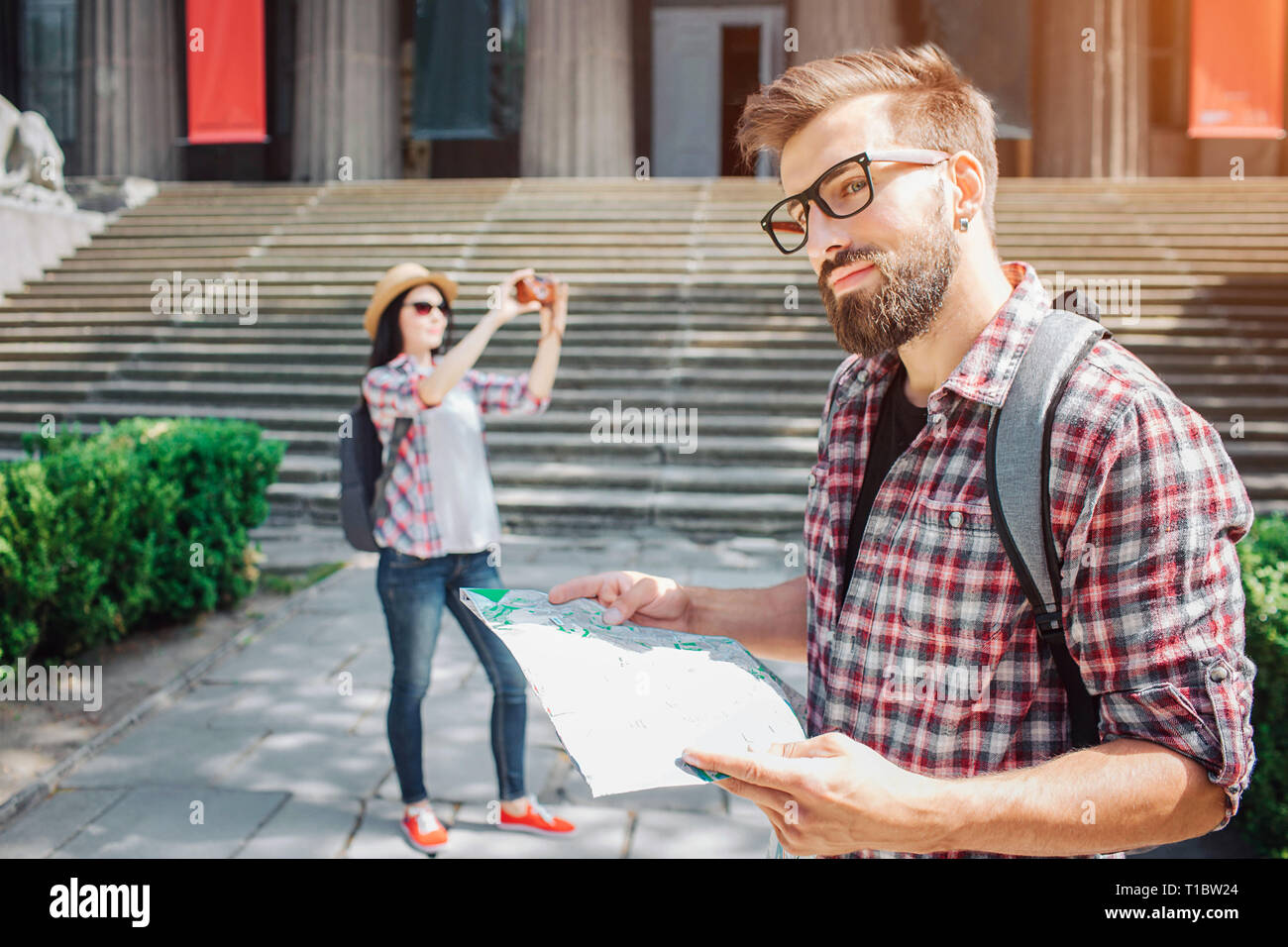 Handsome man stand outside and smile a bit. He holds map in hands ...