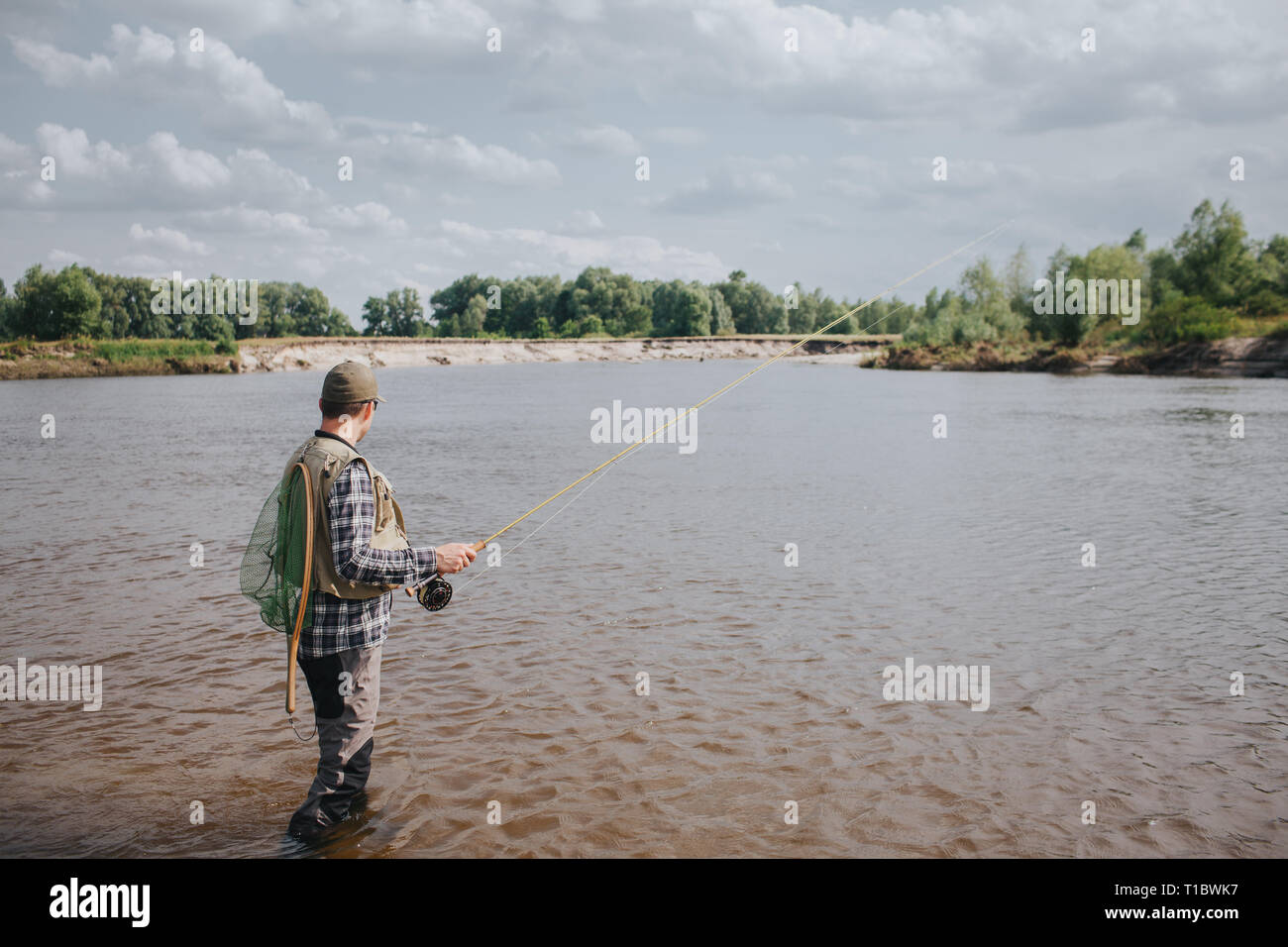 A picture of man standing in water and fishing. He is holding spinning ...