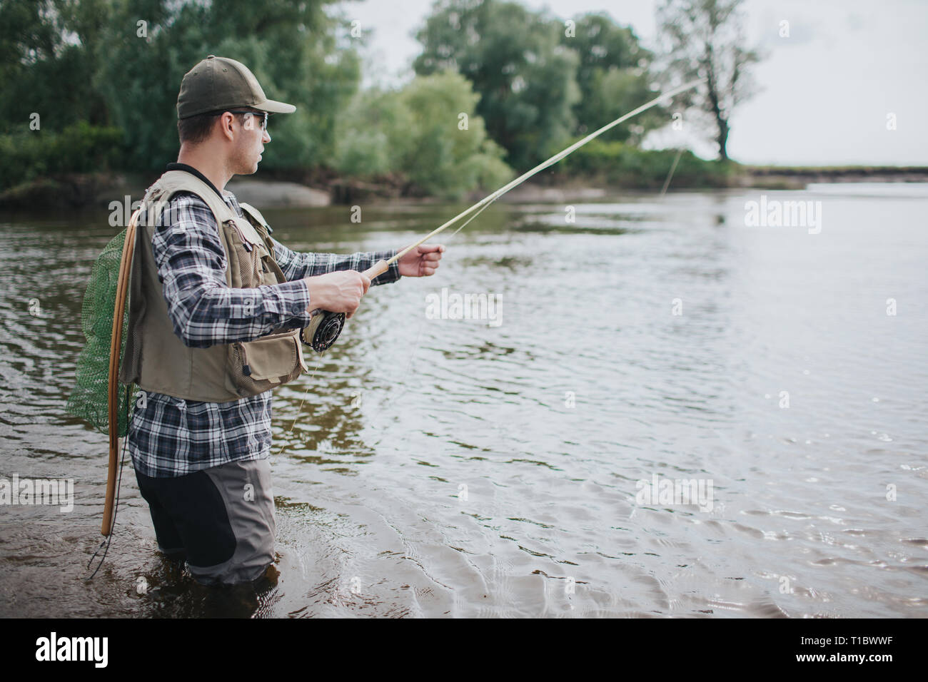 Serious man is standing in water and fishing. He has spinning in hands ...