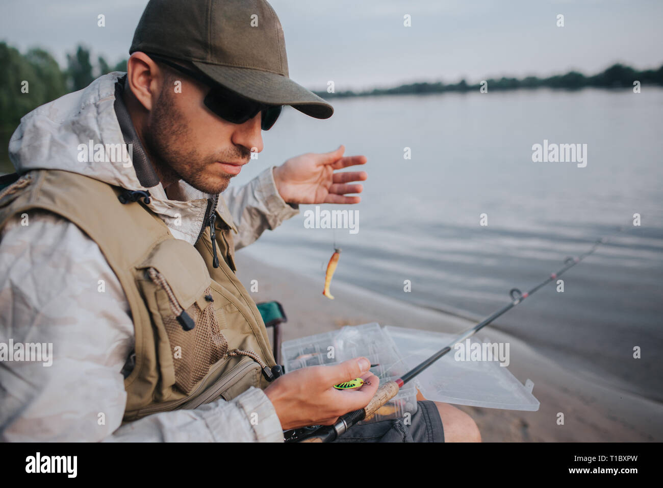 Serious man with sunglasses is sitting at the edge of water and looking ...
