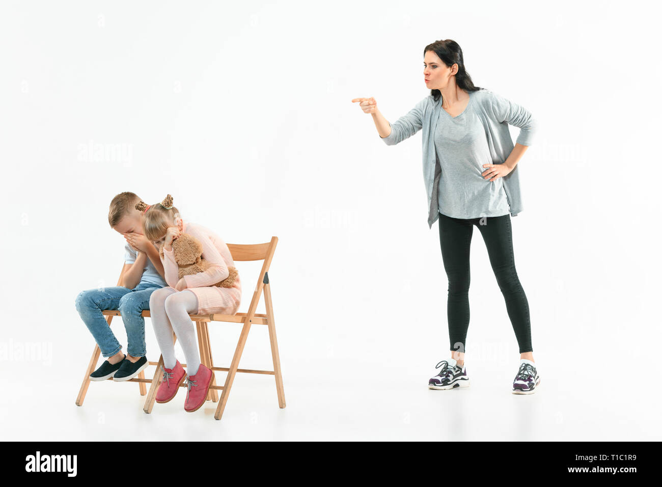 Angry mother scolding her son and daughter at home. Studio shot of emotional family. Human ...