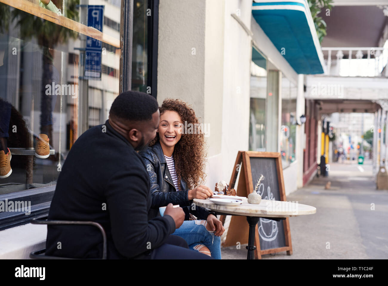 Two smiling friends talking together at a sidewalk cafe Stock Photo - Alamy