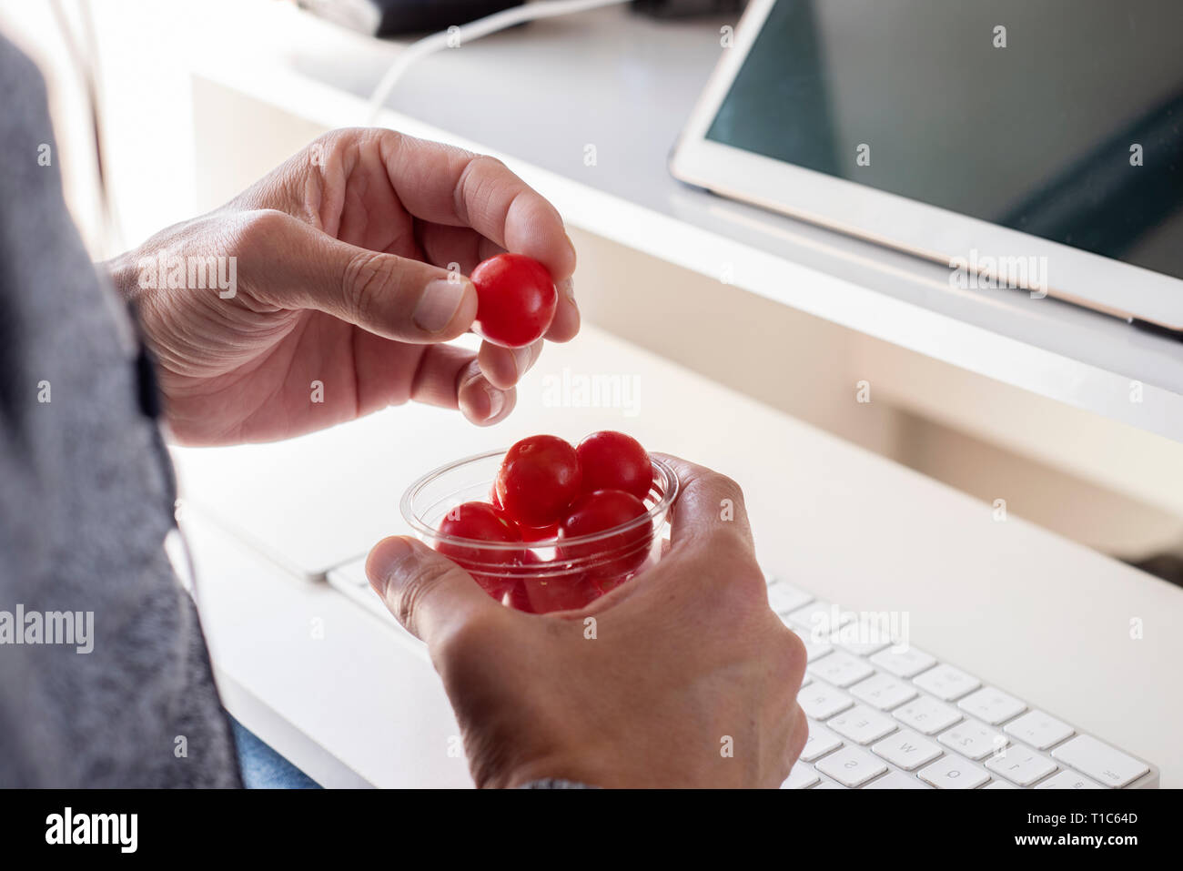 closeup of a young caucasian man eating cherry tomatoes from a plastic ...
