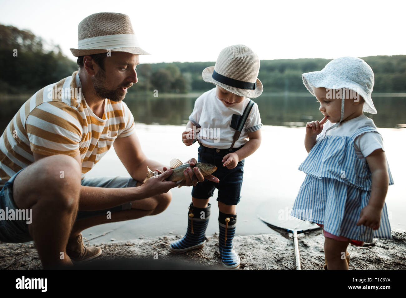A mature father with small toddler children fishing by a lake, holding ...