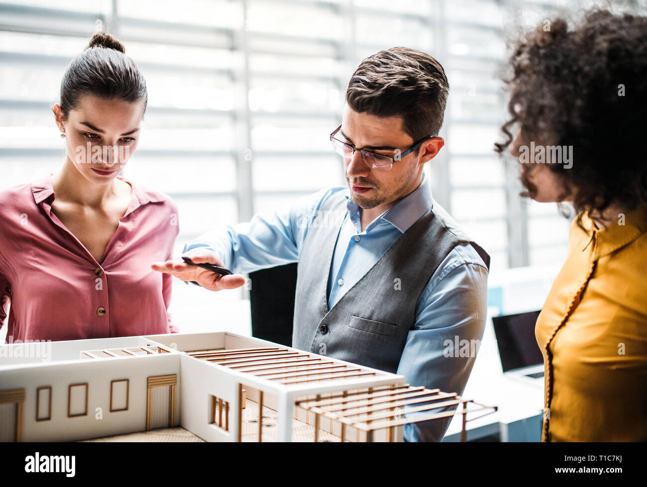 Group of young architects with model of a house standing in office ...