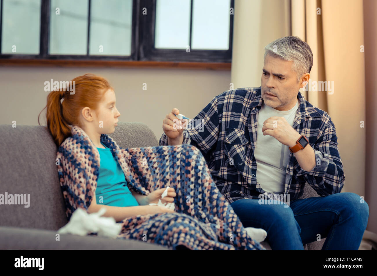 Sad worried father looking at the thermometer Stock Photo - Alamy