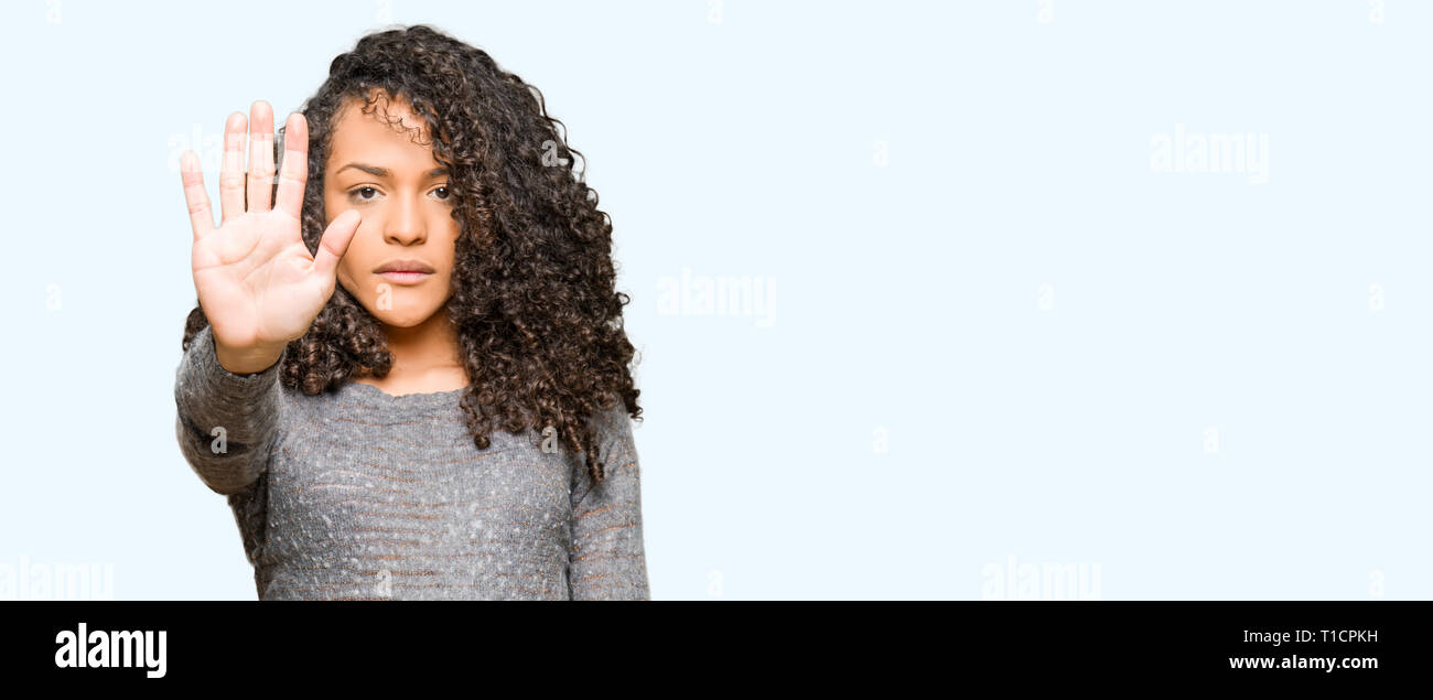 Young beautiful woman with curly hair wearing grey sweater doing stop ...