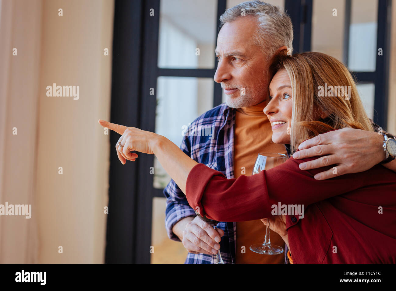Wife pointing on something standing near window with husband Stock ...
