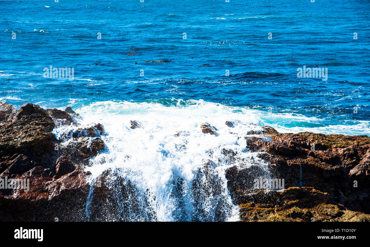 Blue ocean waves breaking against rocks and washing over the rocks ...