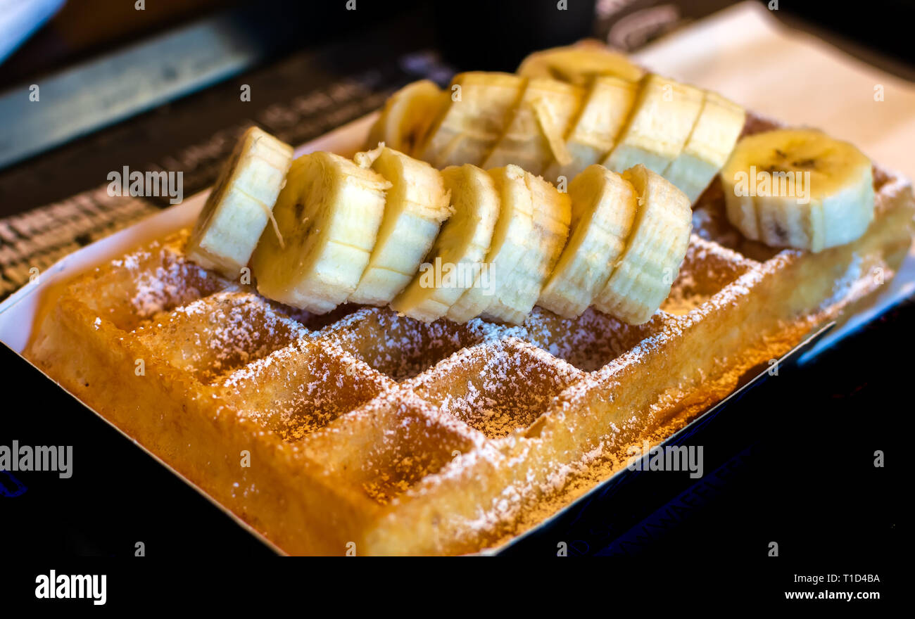 Fresh square Belgian waffle with cut banana topping and sugar powder ...