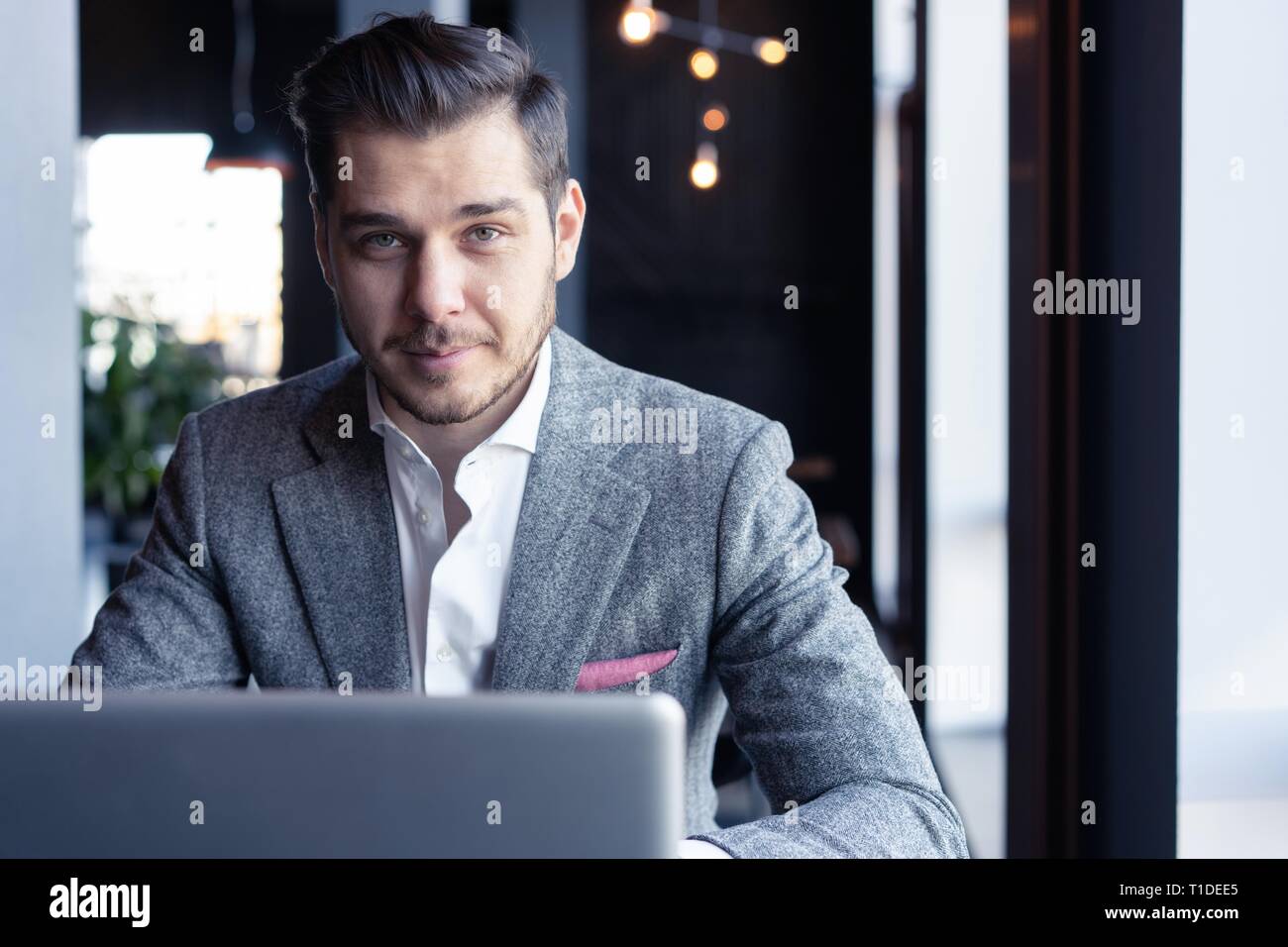 Good looking young man in full suit using computer while sitting in the ...