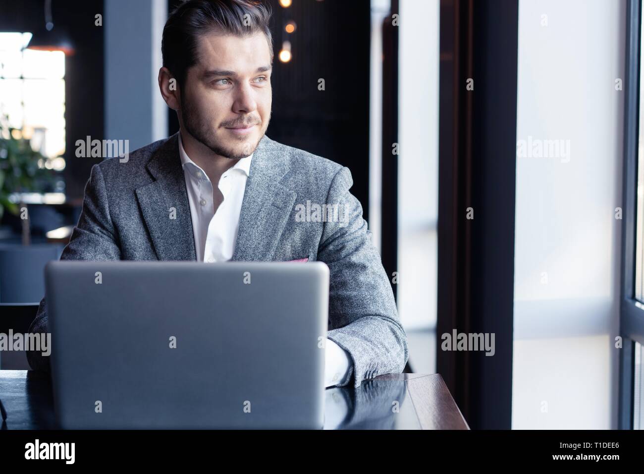 Good looking young man in full suit using computer while sitting in the ...