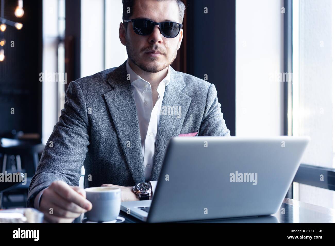 Good looking young man in full suit using computer while sitting in the ...