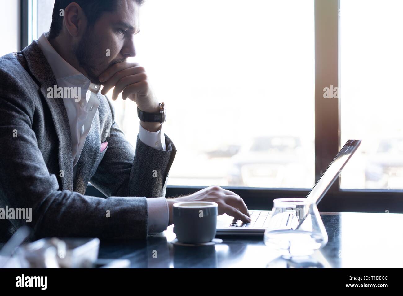 Good looking young man in full suit using computer while sitting in the ...