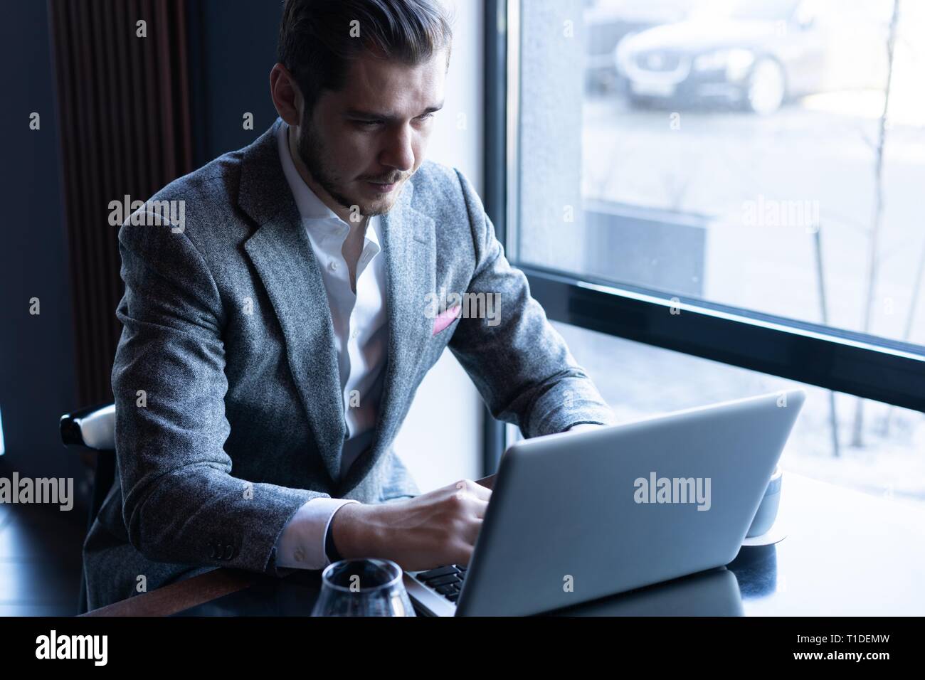 Good looking young man in full suit using computer while sitting in the ...