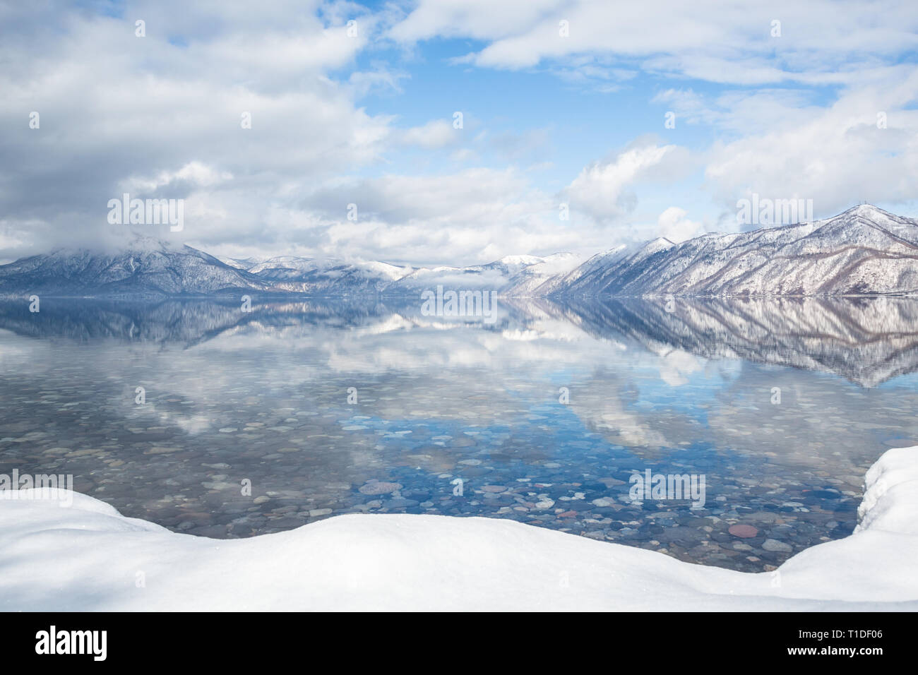 Snow on the shore of a shallow lake with smooth rocks and distant peaks ...