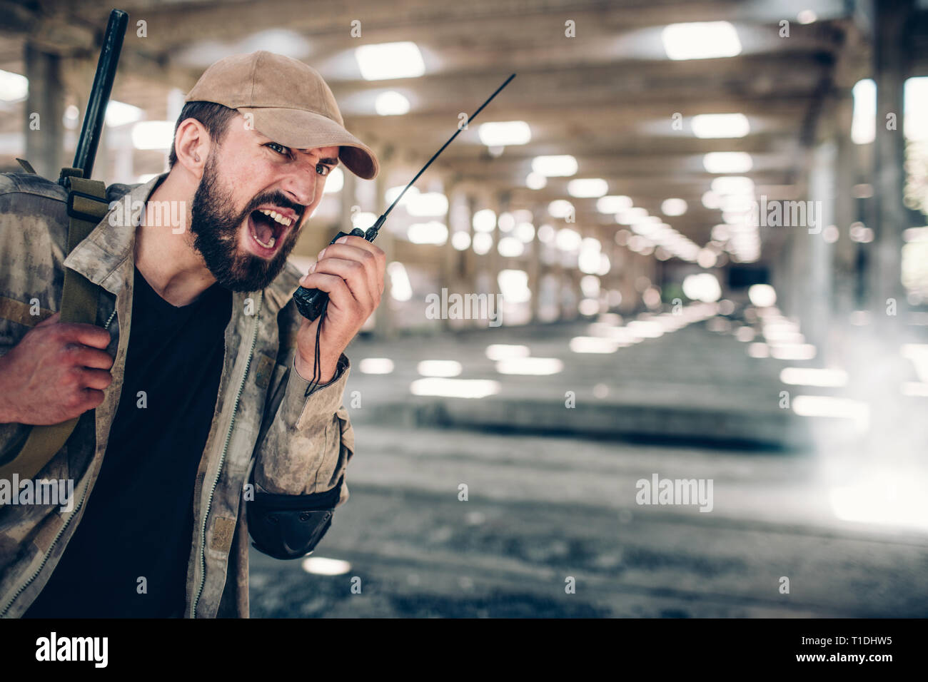 Cut view of soldier screaming in portable radio. Big rifle is hanging ...