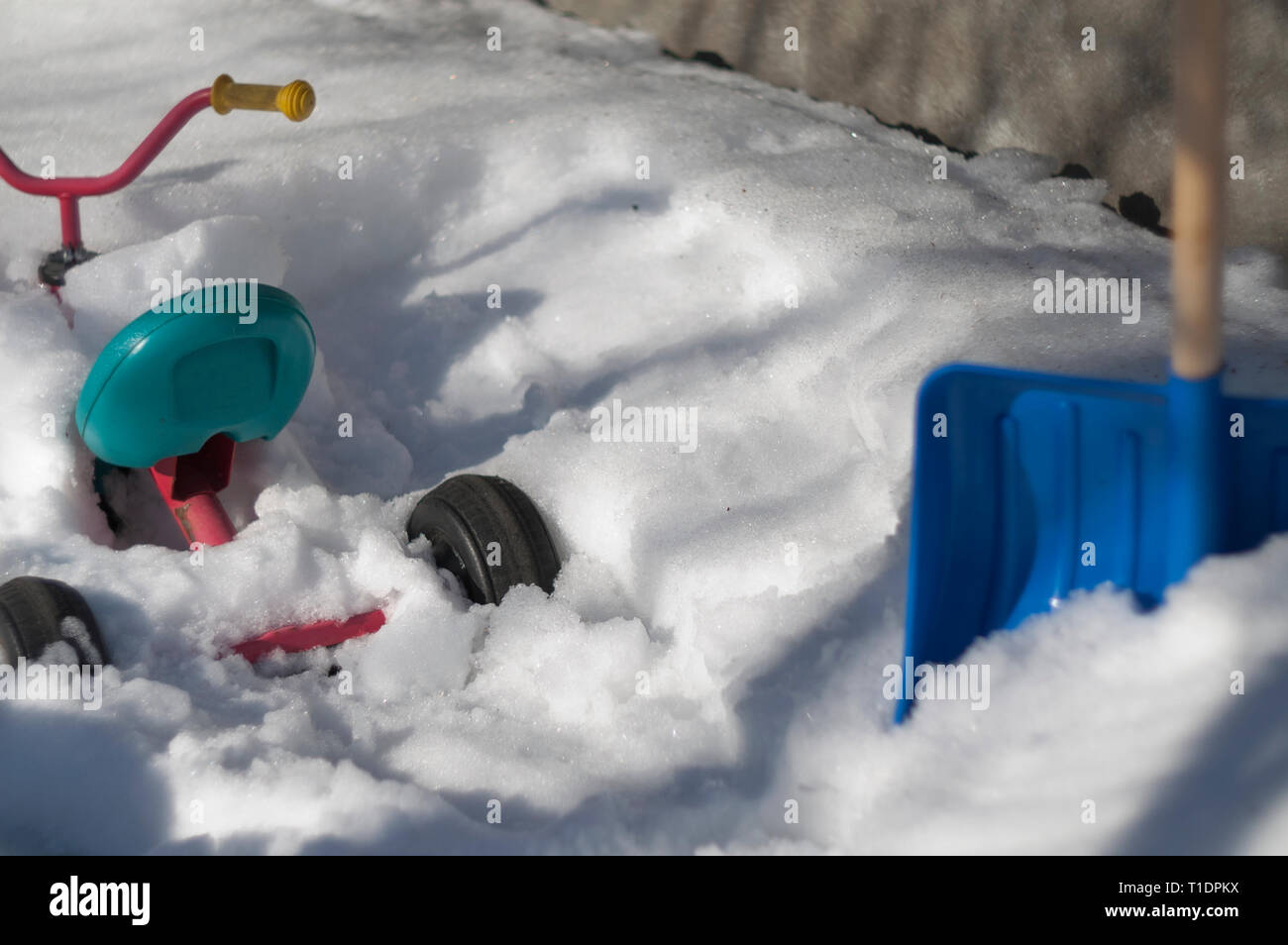 Children bicycle and shovel in the snow piles, outdoor sunny day shot ...