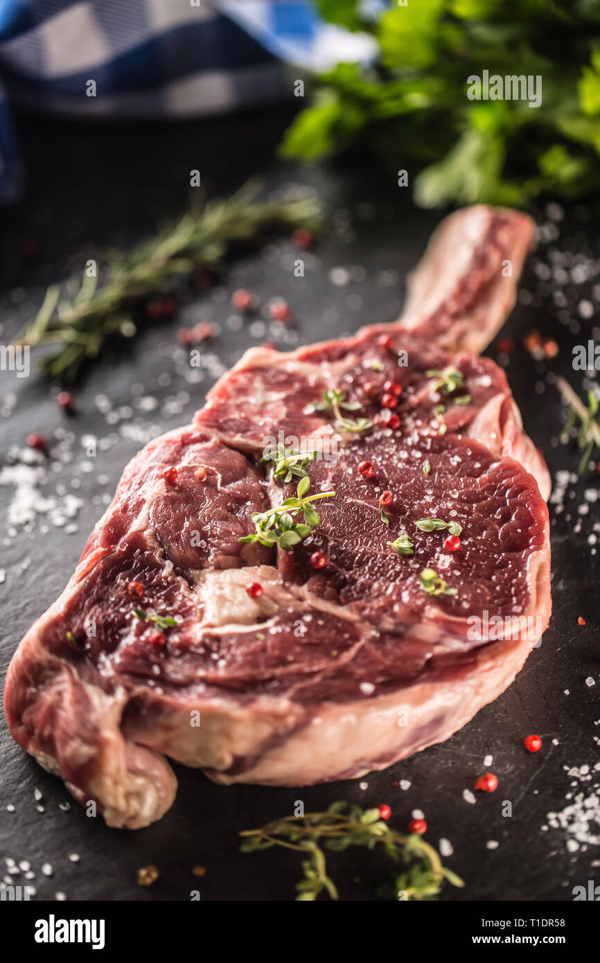 Raw beef tomahawk steak with salt pepper and rosemary on slate plate ...