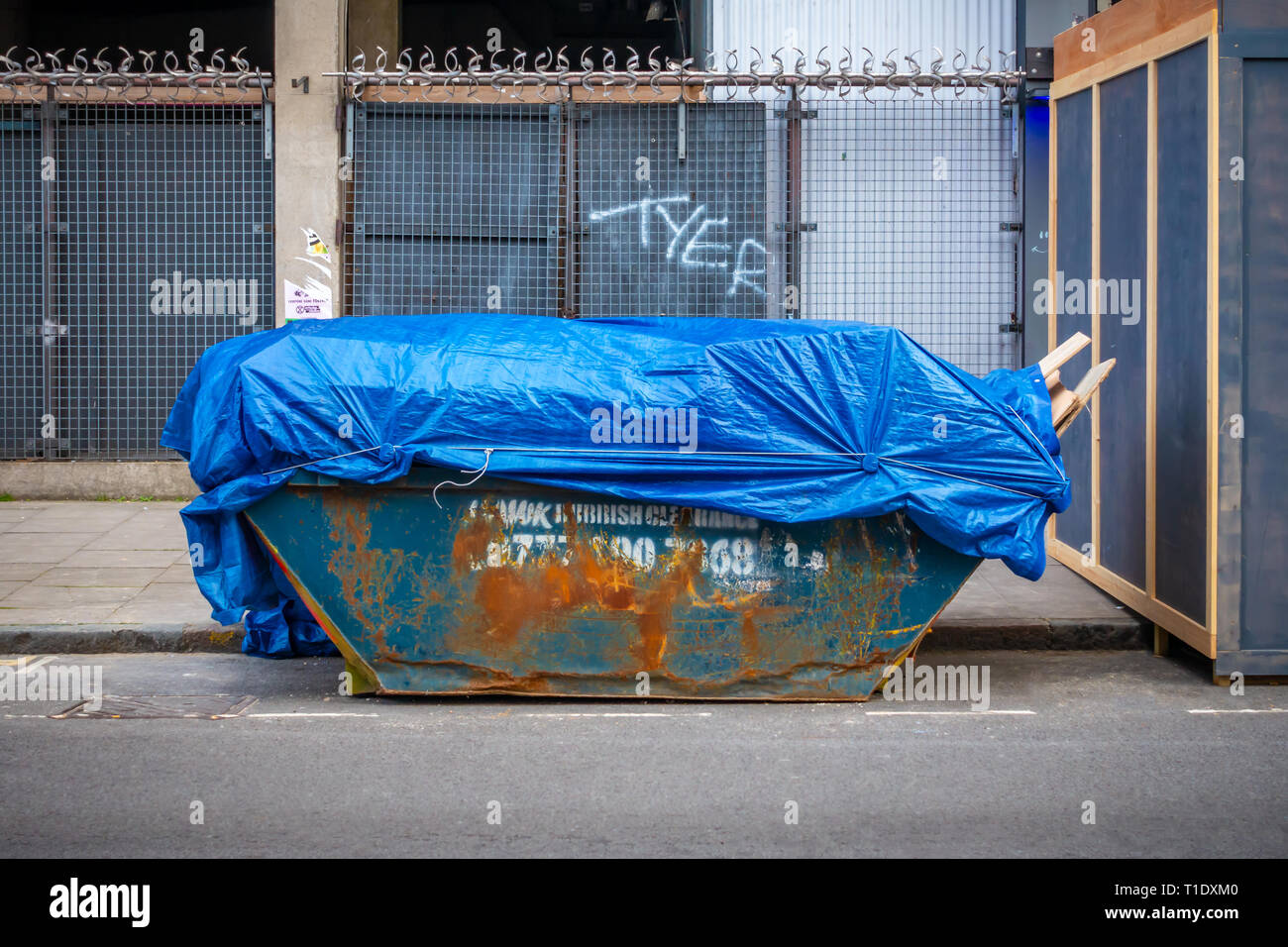 blue plastic tarp cover covering a full construction builders skip ...