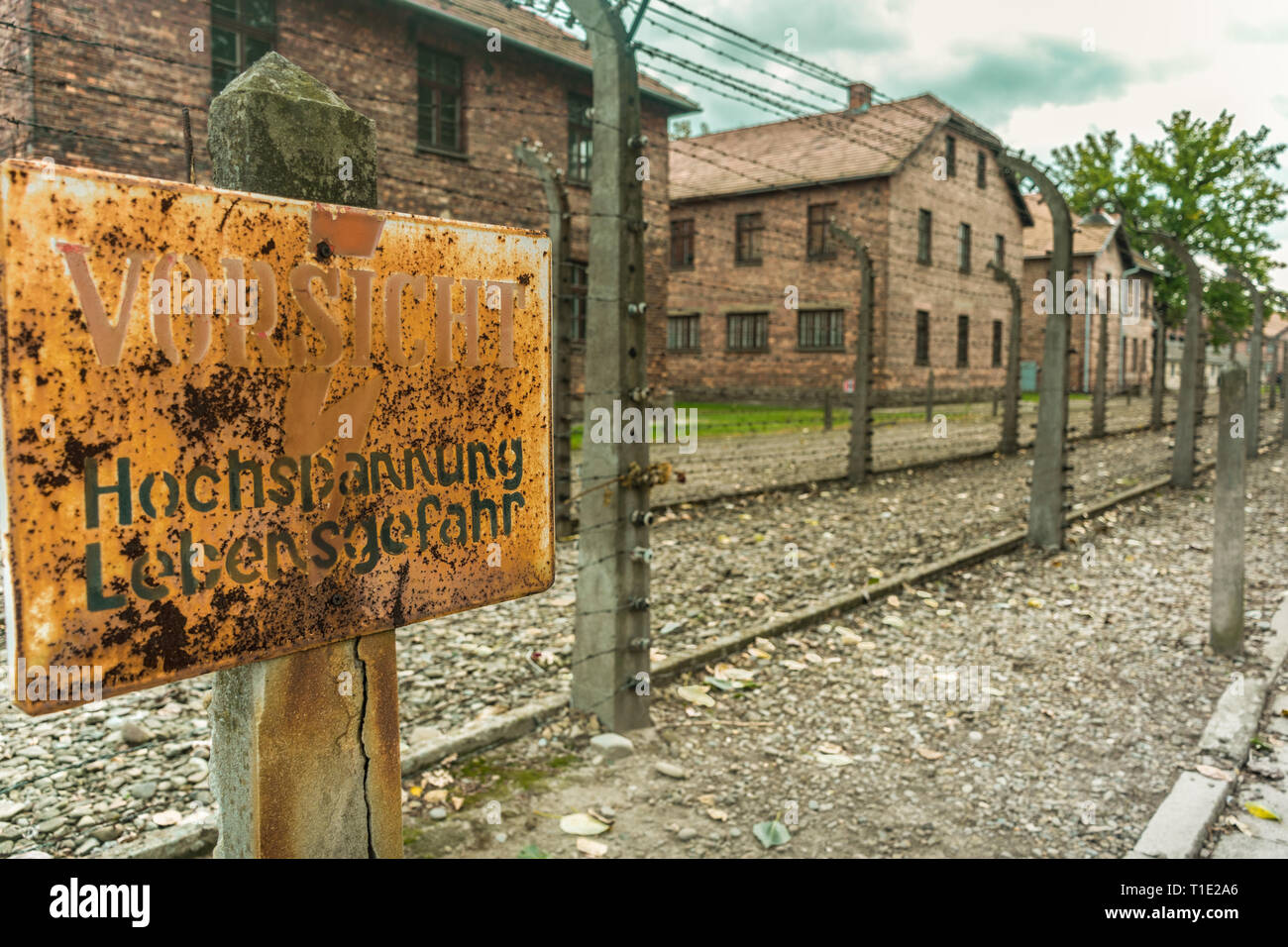 Old rusty plate warning sign indicating electric fence with barbed wire ...