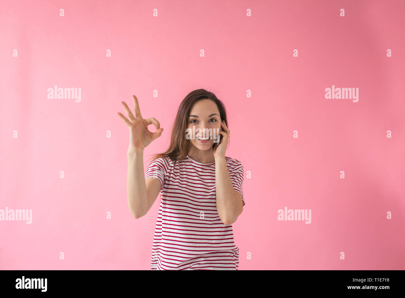Positive beautiful young girl uses a cell phone and shows a hand sign ...