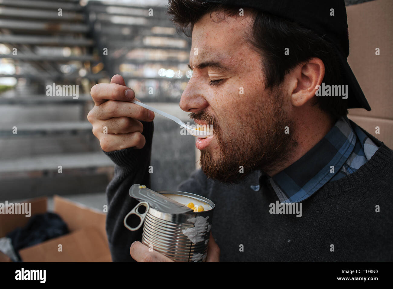 homeless and poor. Guy is eating corn from can. He is keeping his eyes ...