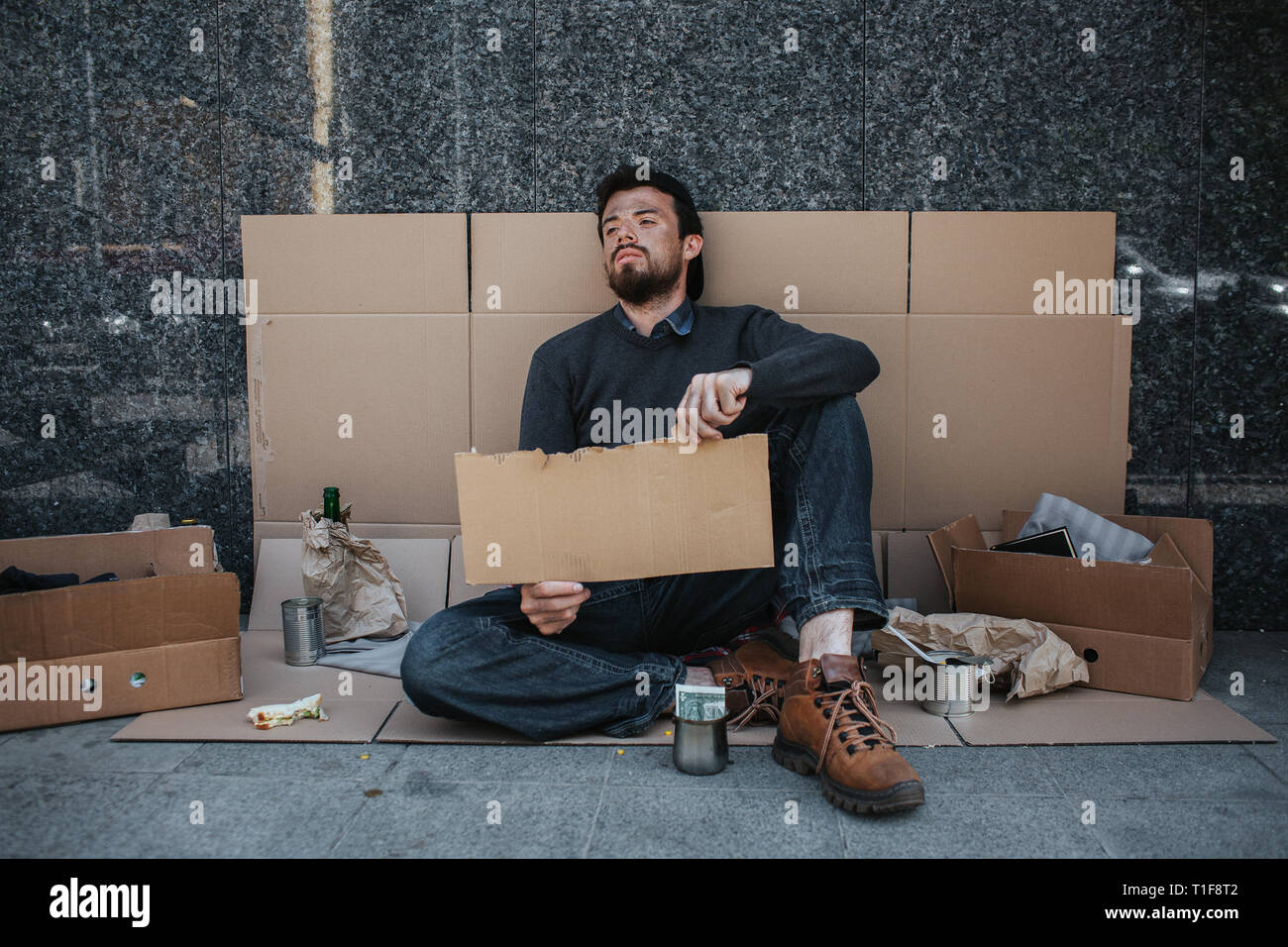 Hopeless and homeless person is sitting on cardboard on the ground and ...