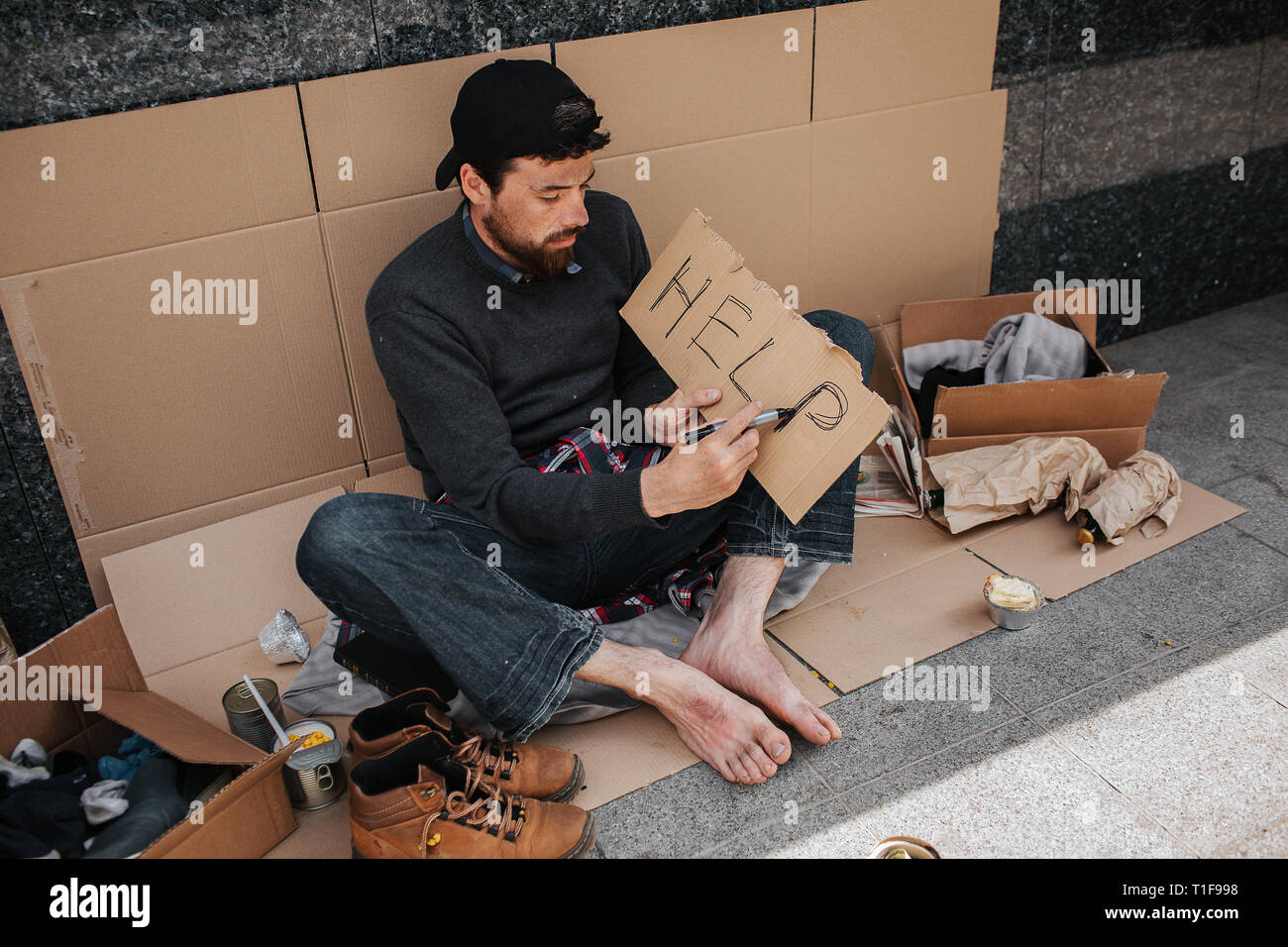Dirty homeless man is sitting on cardboard and writing down the word ...