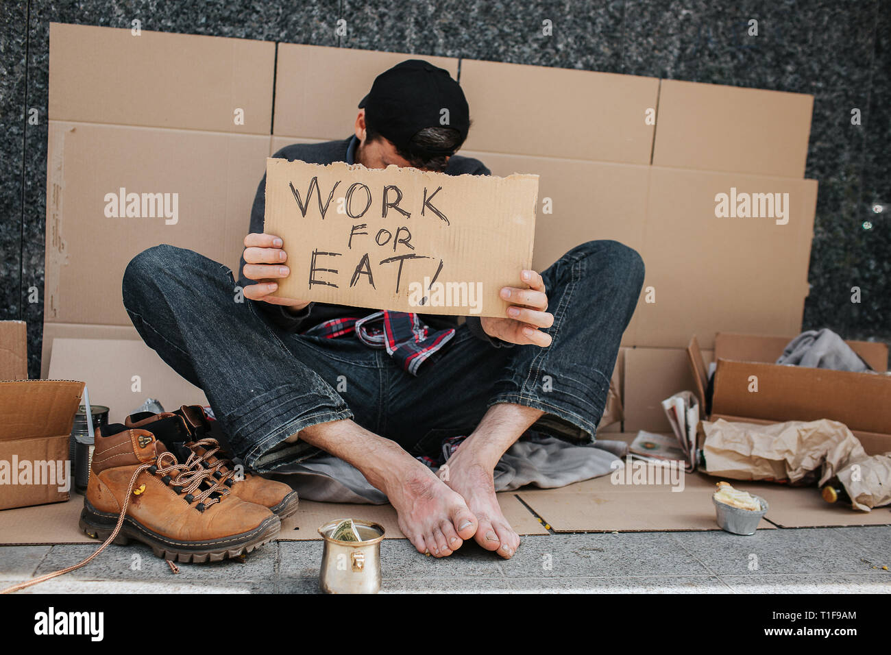 Jobless guy is sitting on the concrete ground and covering his face ...