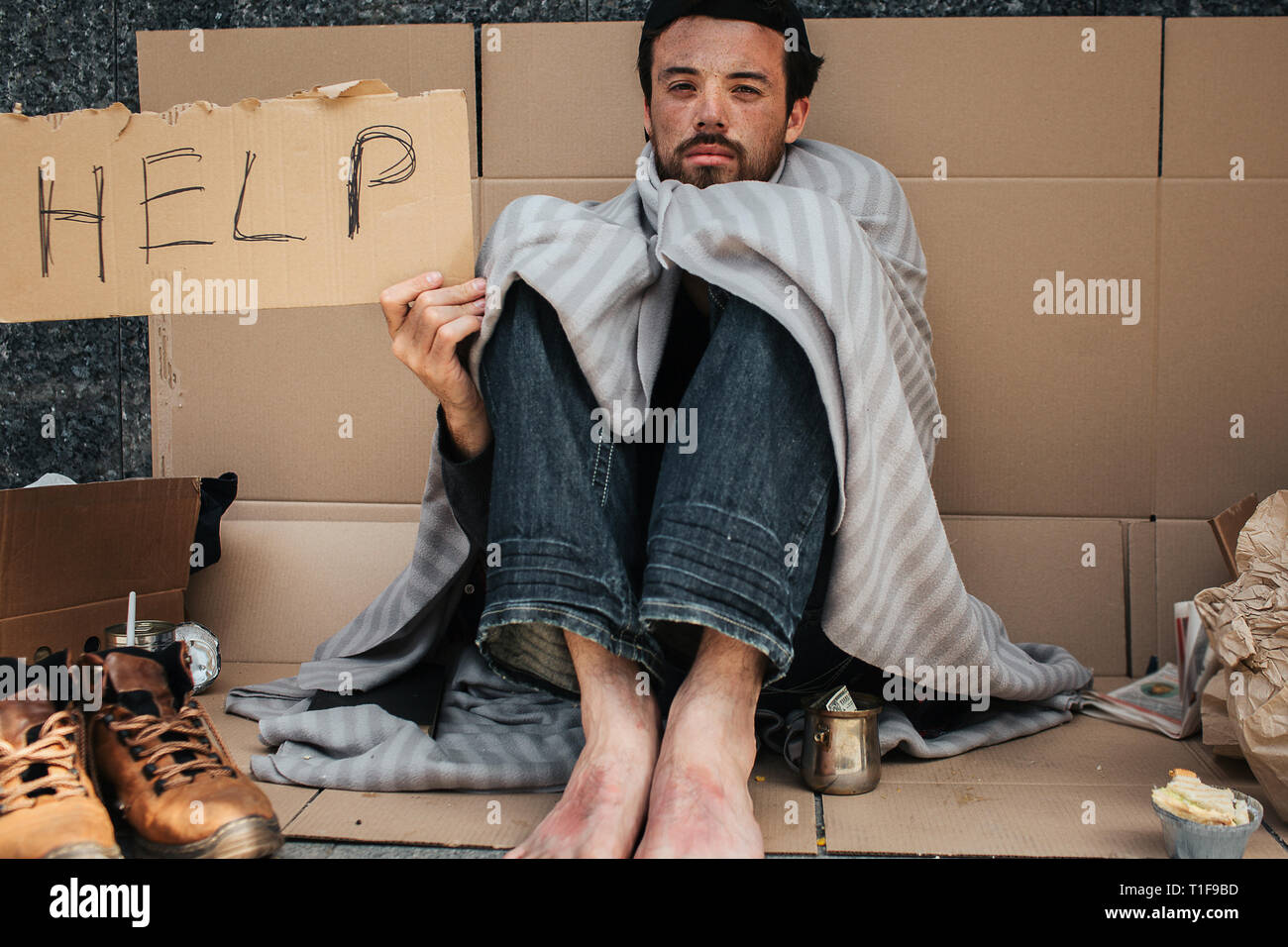 Guy is sitting on the ground and freezing. He has a tiny blanket on his ...