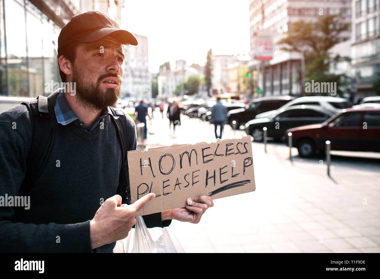 Guy is standing on the street and pointing on piece of cardboard which ...