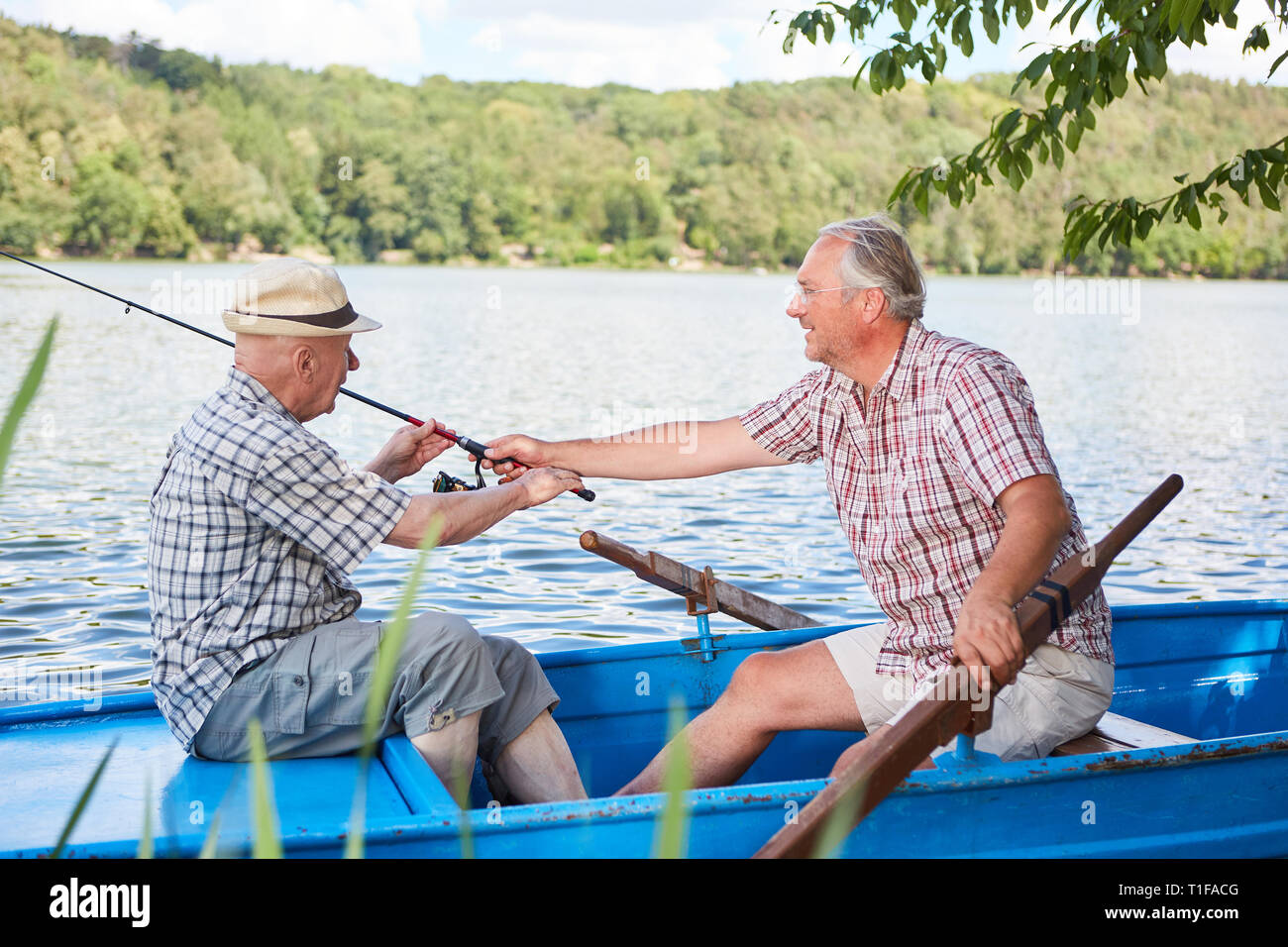 Two seniors in a rowing boat at the lake together while fishing as a ...