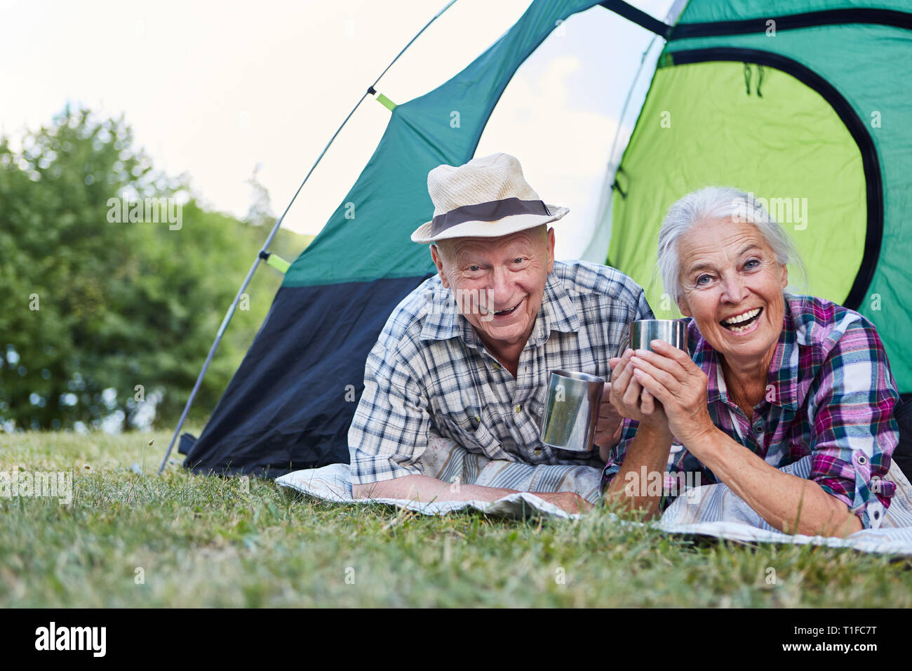 Laughing couple seniors in tent with a cup of coffee on camping holiday ...