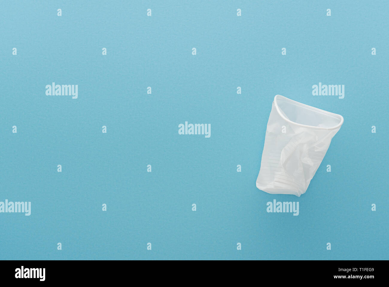 top view of white and crumpled plastic cup on blue background with copy ...