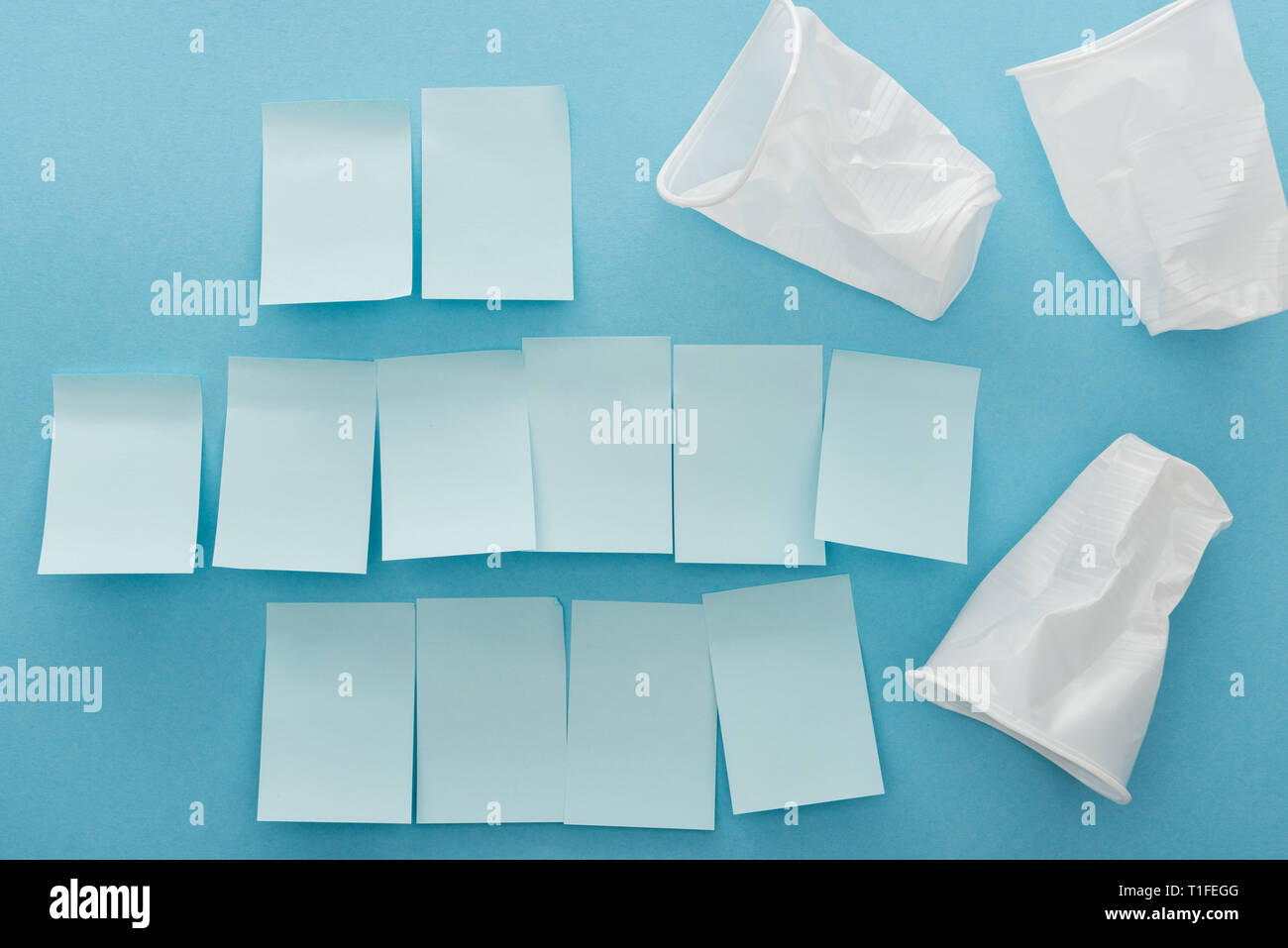 top view of white plastic and crumpled cups and empty sticky notes on ...