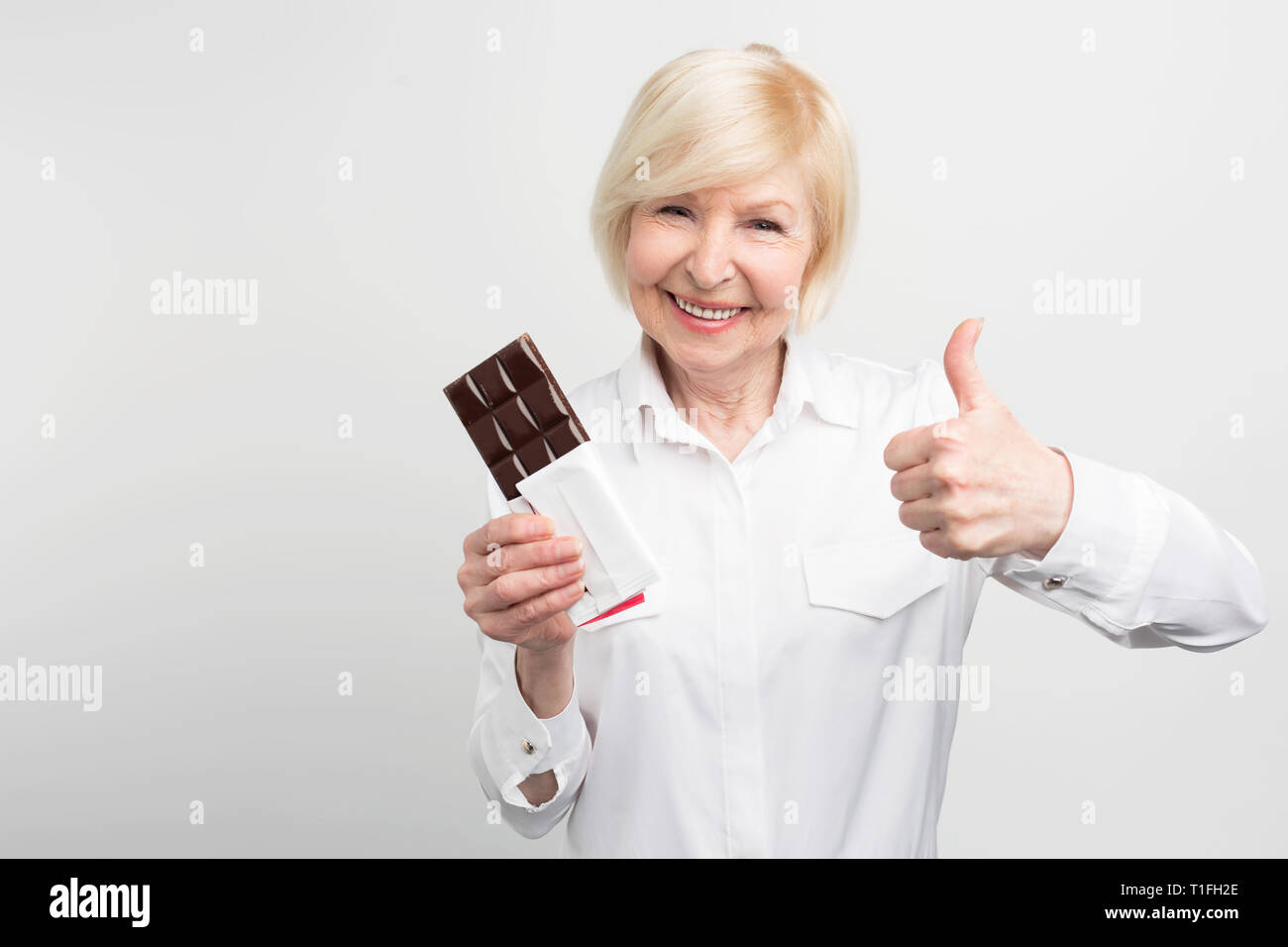 Old lady is holding a bar of good chocolate and looking straight ahead ...