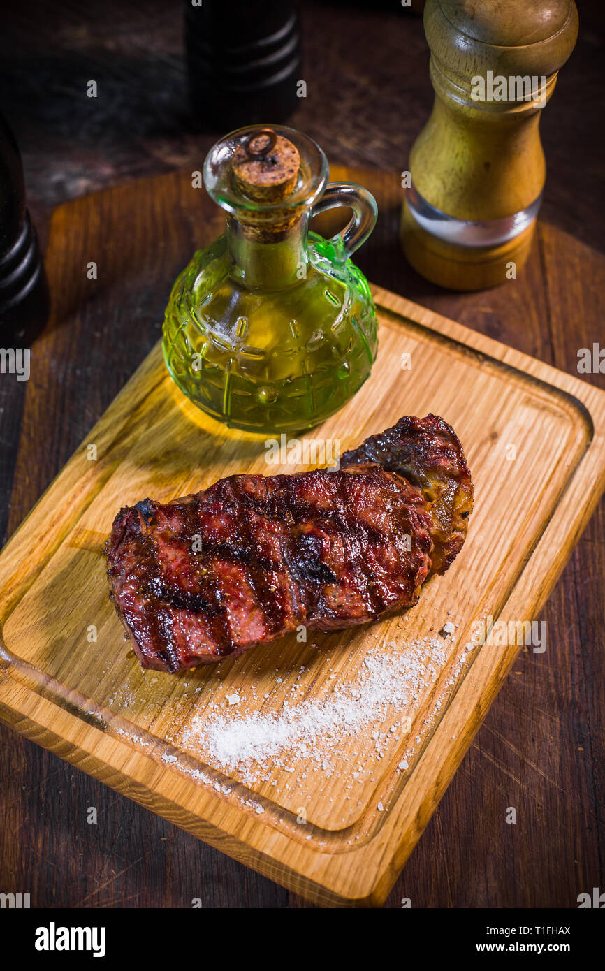 Grilled pork rib chop steak in a clay plate with oil, mustard, salt and ...