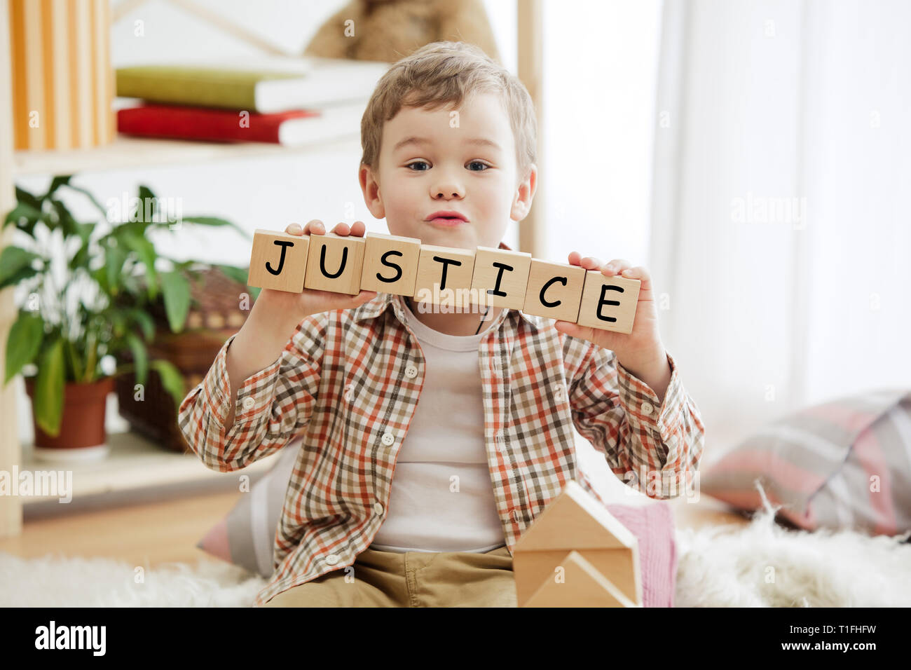 Wooden cubes with word justice in hands of little boy at home ...