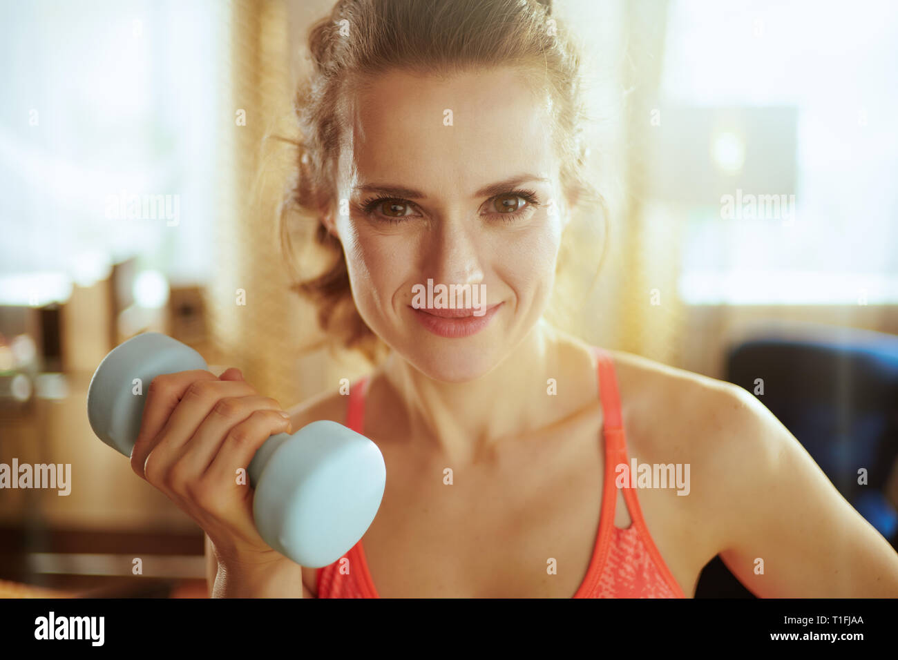 Portrait of happy healthy woman in fitness clothes with dumbbell in the ...