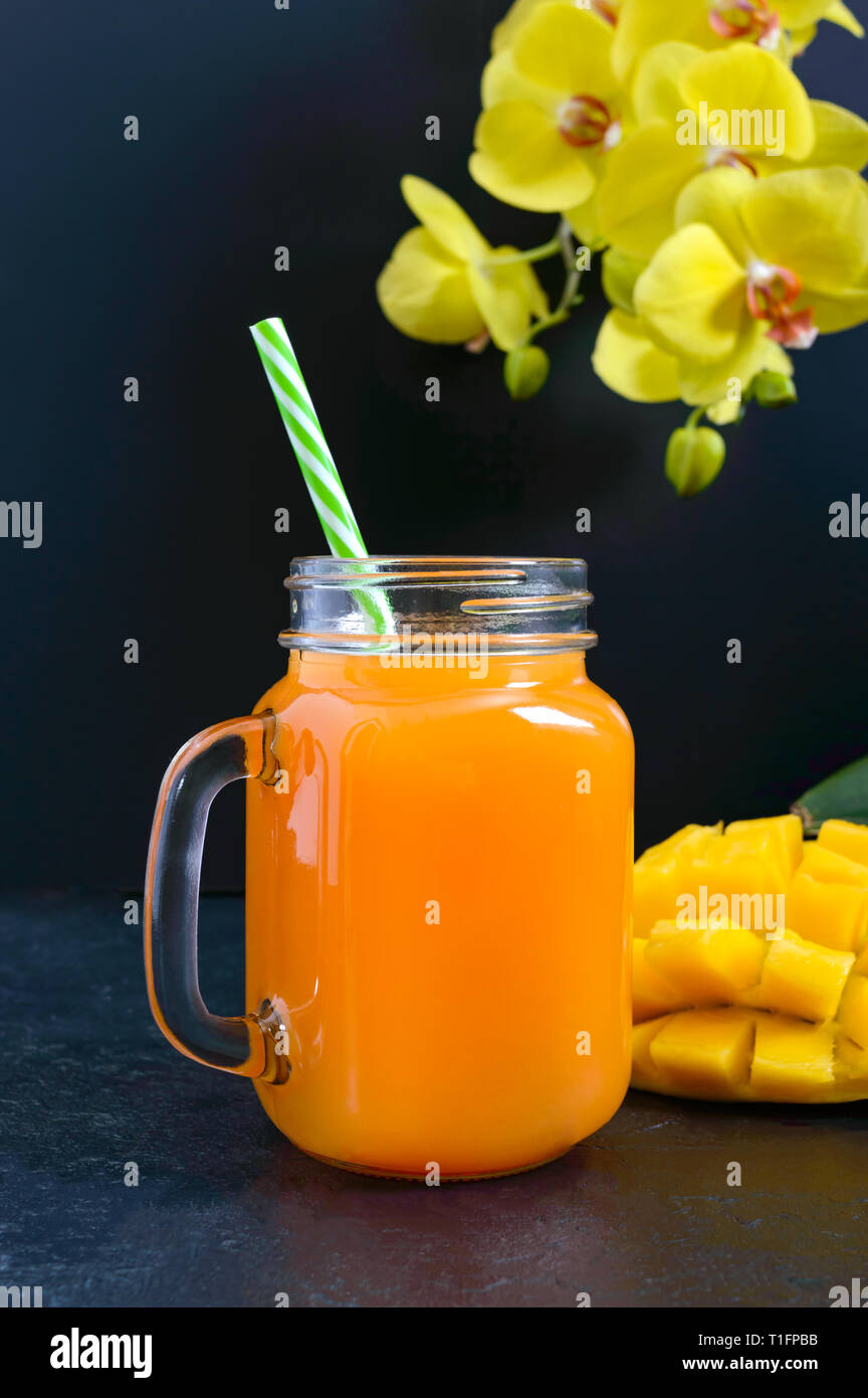 Mango smoothie in a glass jar and fresh mango on a black background ...