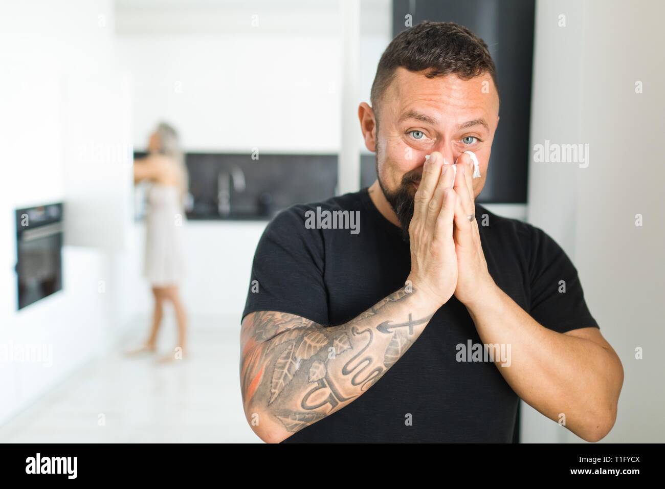 Man in kitchen having hay fever using tissue paper to clear nose Stock ...