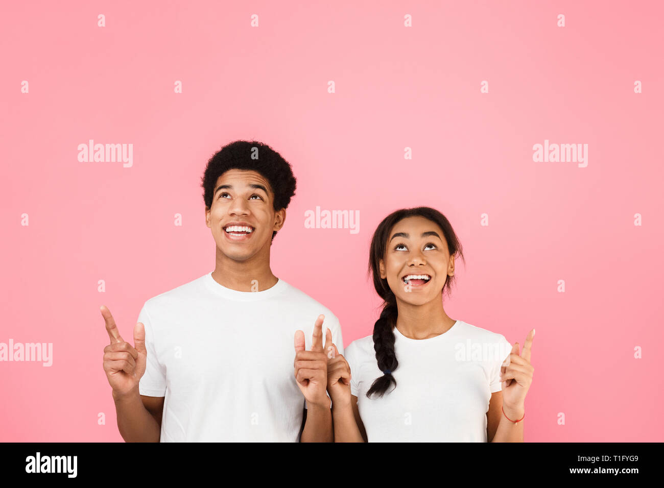 Happy students pointing and looking up on pink background Stock Photo ...
