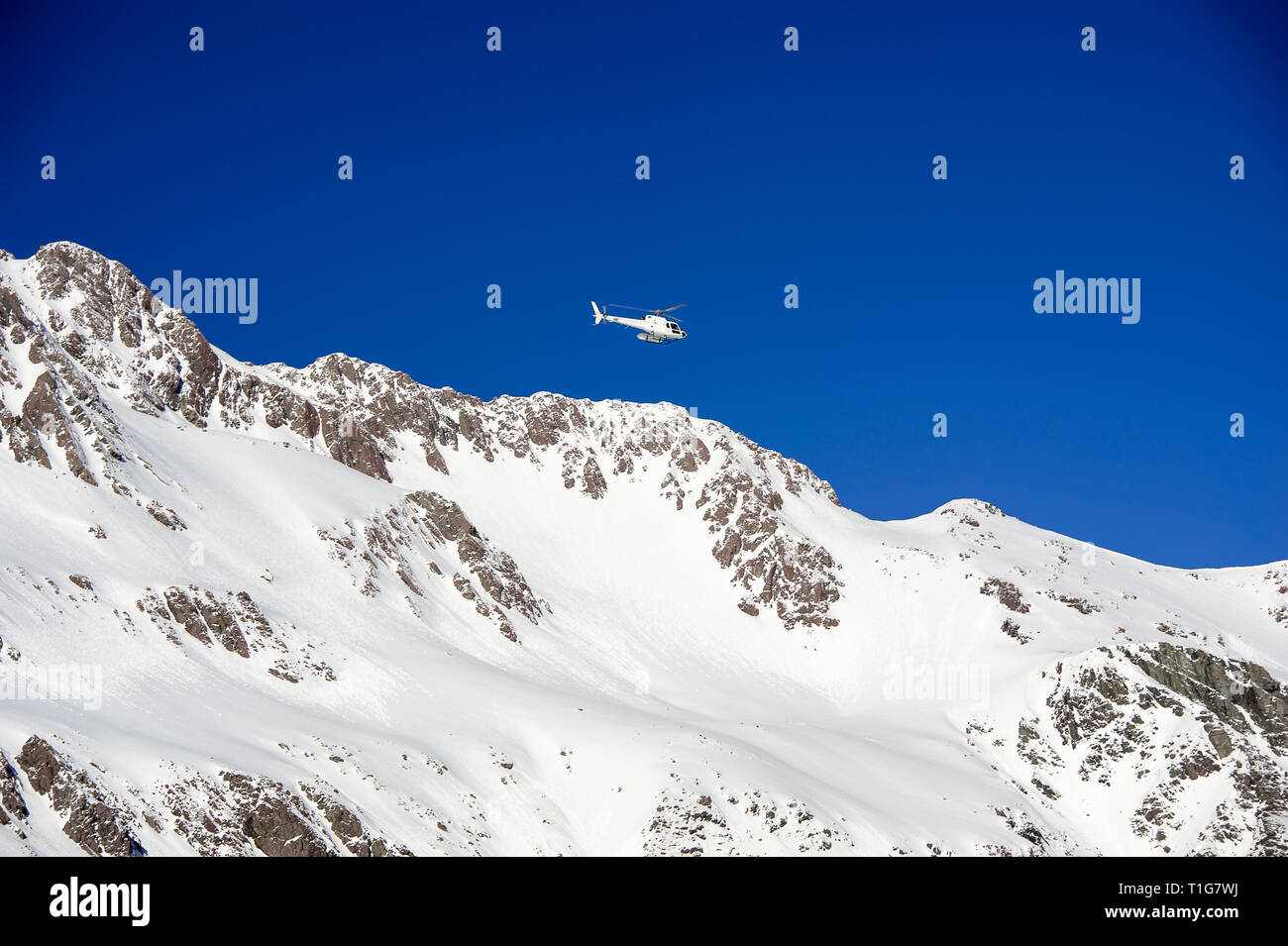 Helicopter flying over the top of snow covered mountains. White ...