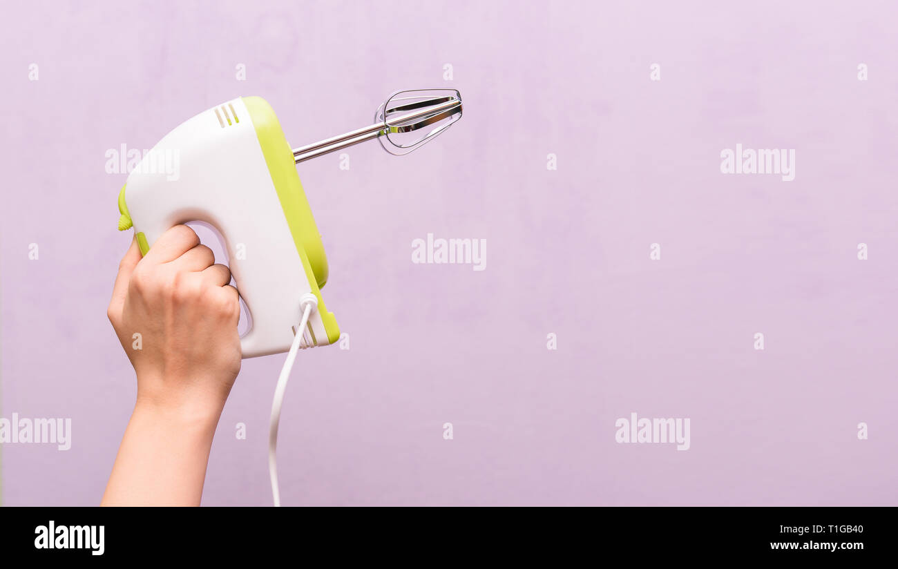 Female hand is holding a mixer. Kitchen electric appliance on a purple ...