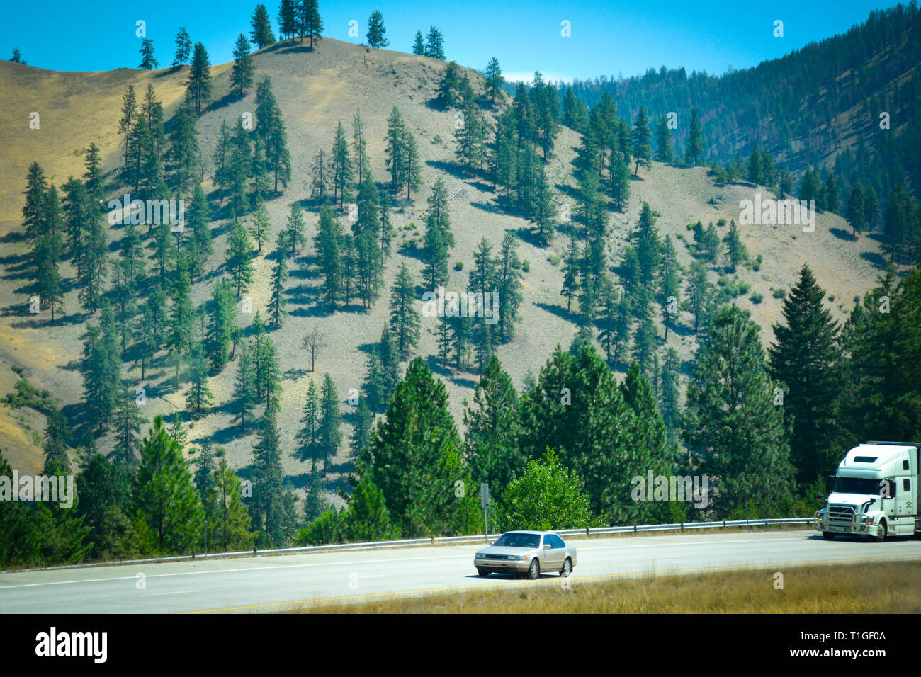 A car and a semi-truck climb a grade uphill on I-90 interstate freeway ...