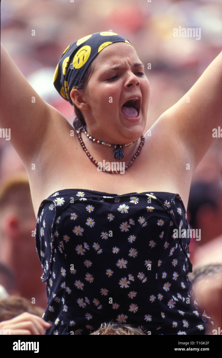 A concert fan on shoulder top is shown cheering with her arms held ...